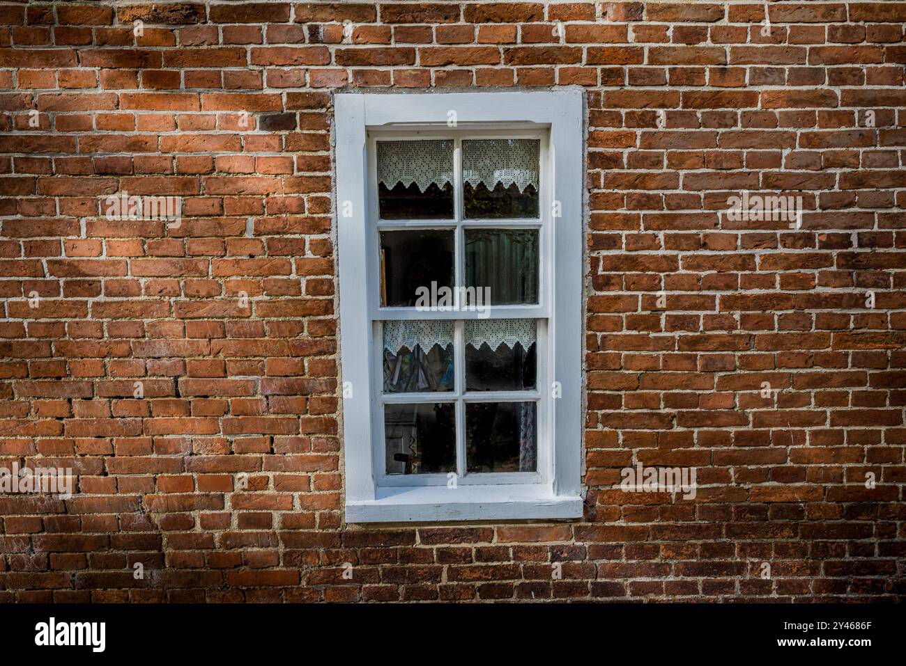 Old fashioned window with white frame and lace curtains on a red brick ...