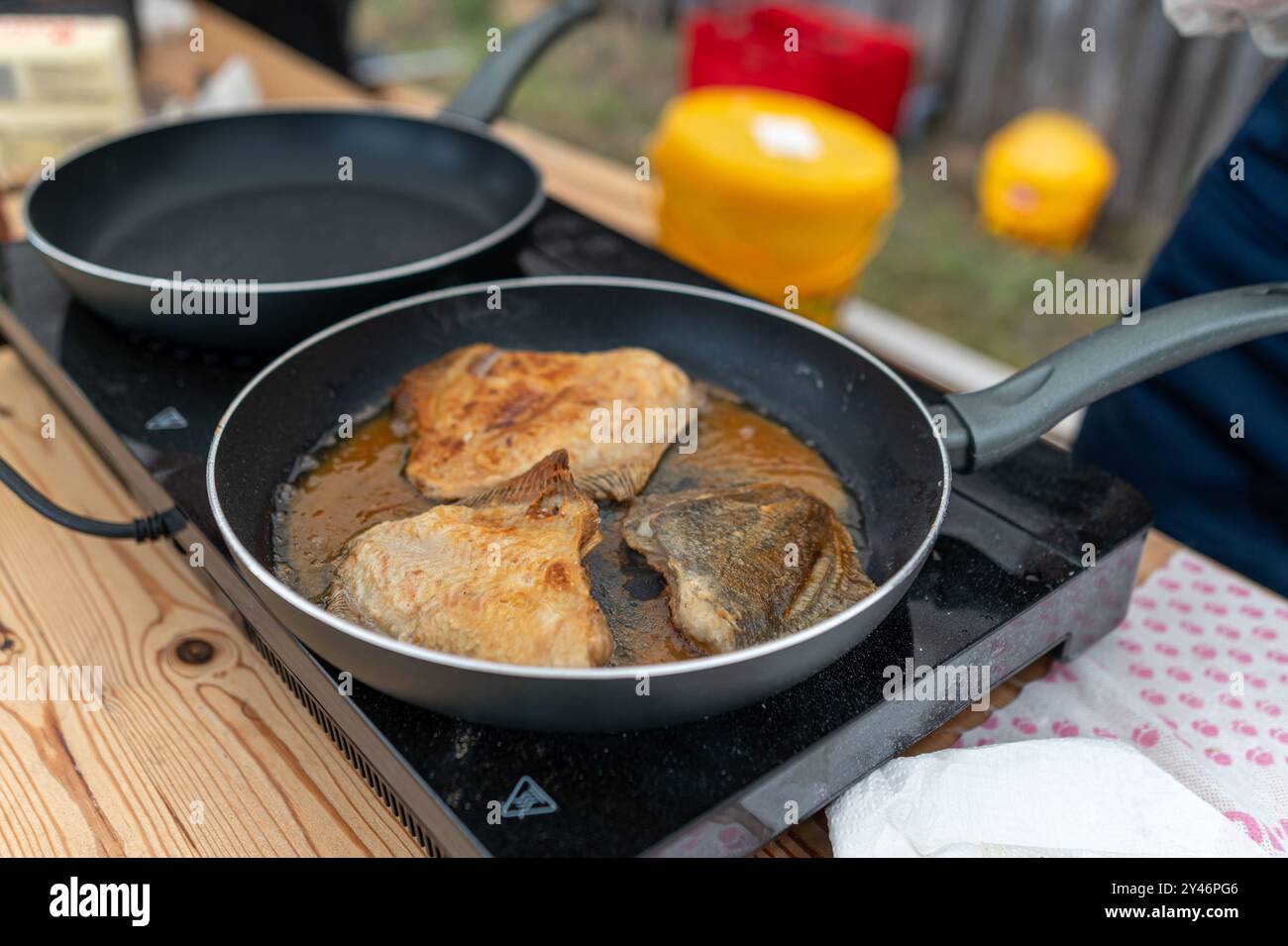 Fish fillets sizzle in a frying pan on a portable stove during a lively ...