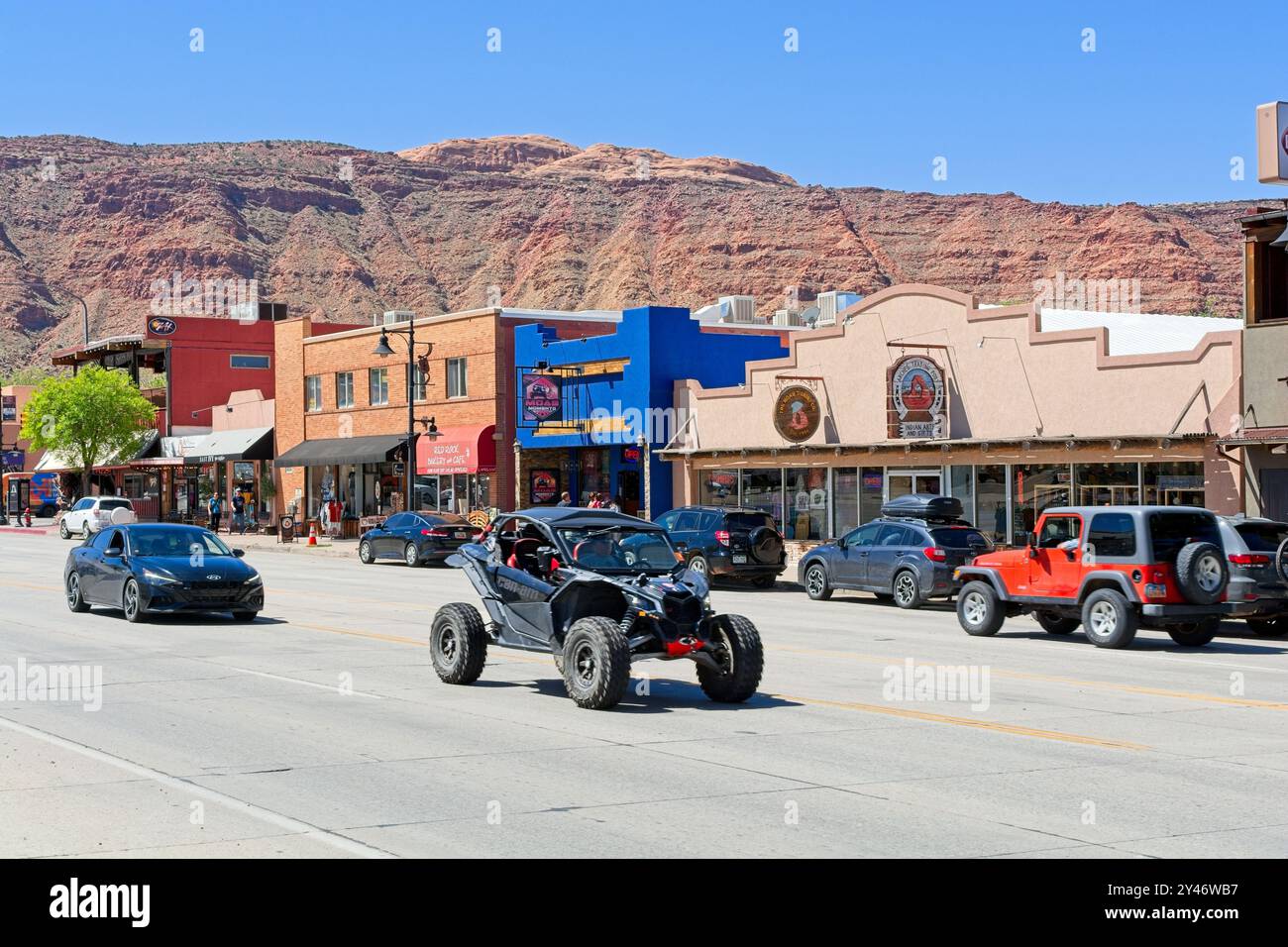 Off road vehicle traveling down Main Street with red Moab rim cliffs ...