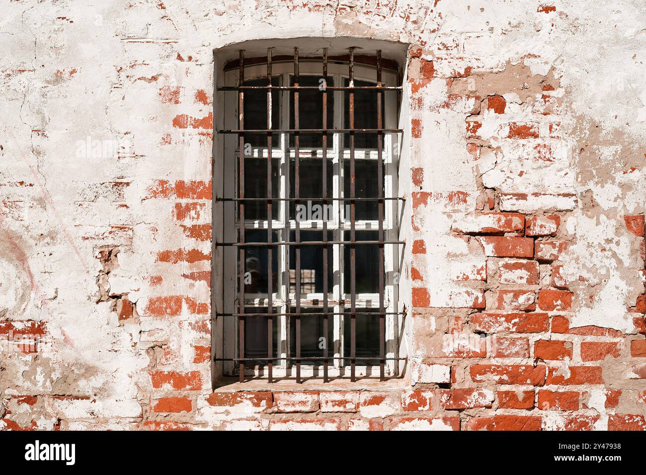 Barred window of an old prison on a white brick wall. Jail and imprisonment concept. Old damaged ...