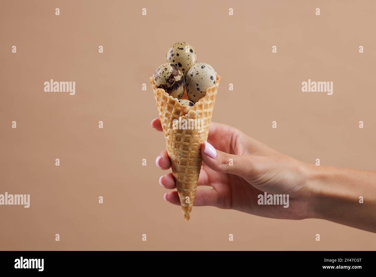Hand holding waffle cone filled with quail eggs.on beige background ...
