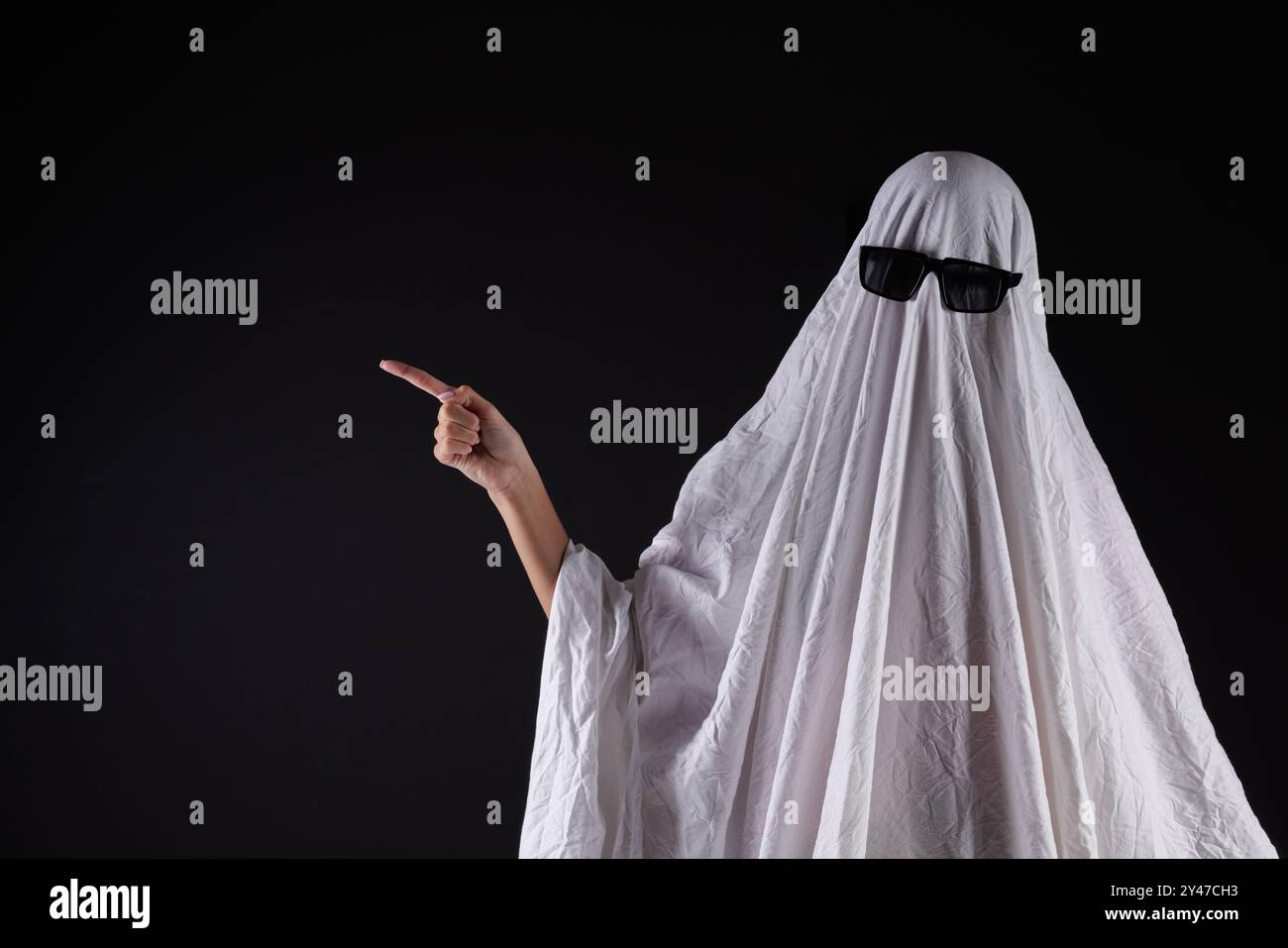 Person in costume of ghost pointing at something on dark background ...