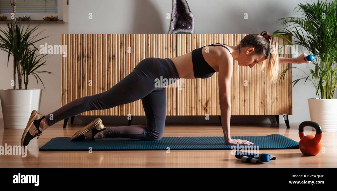 Profile view of a fit young woman exercising on a yoga mat at home in ...