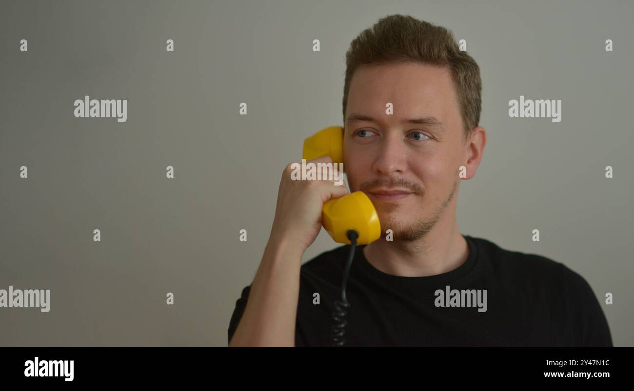 A man talking on the phone with a yellow retro telephone receiver ...