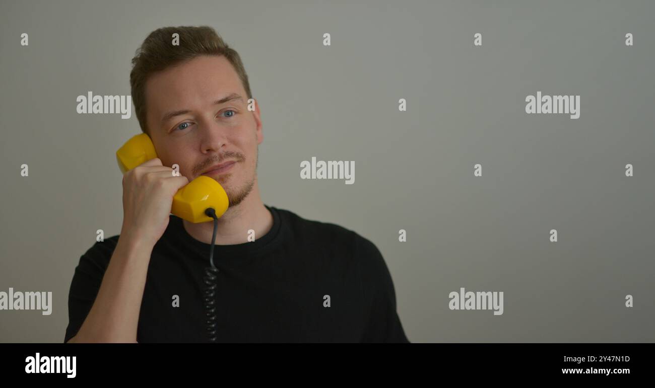 A man talking on the phone with a yellow retro telephone receiver ...