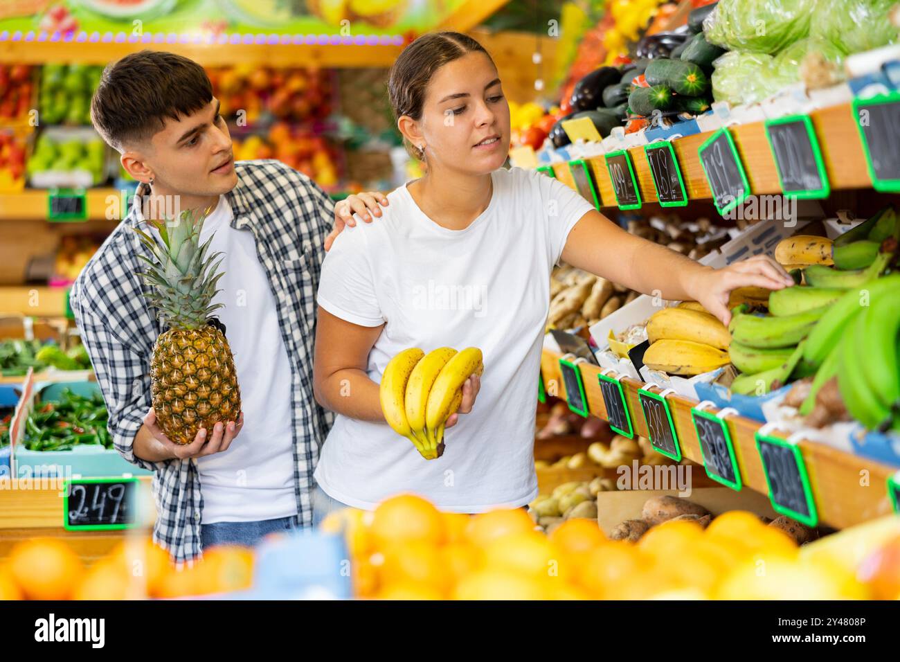 Young positive couple choosing fresh organic fruits in supermarket ...