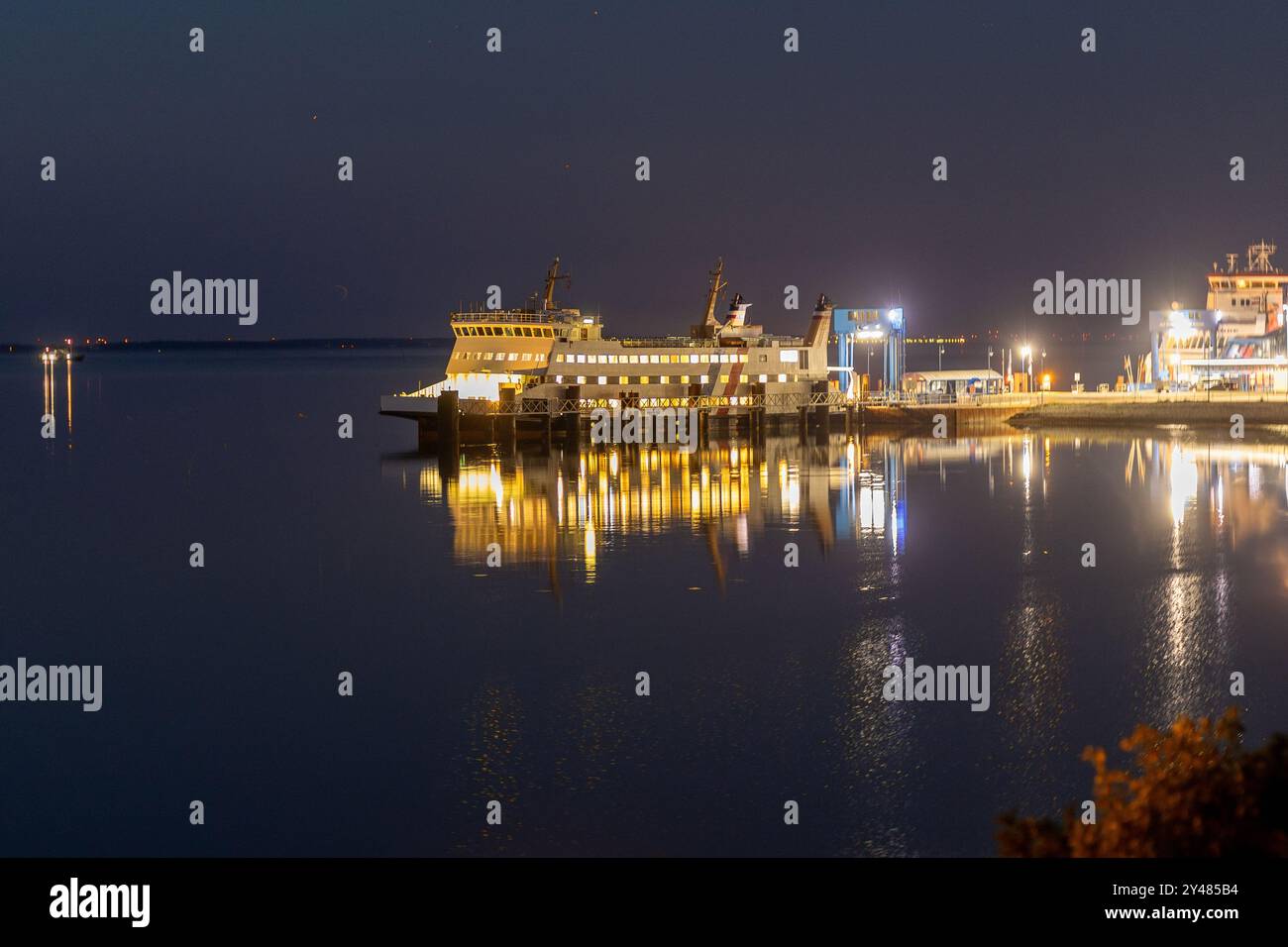 A ferry sits at a bustling harbor at night, illuminated by vibrant ...