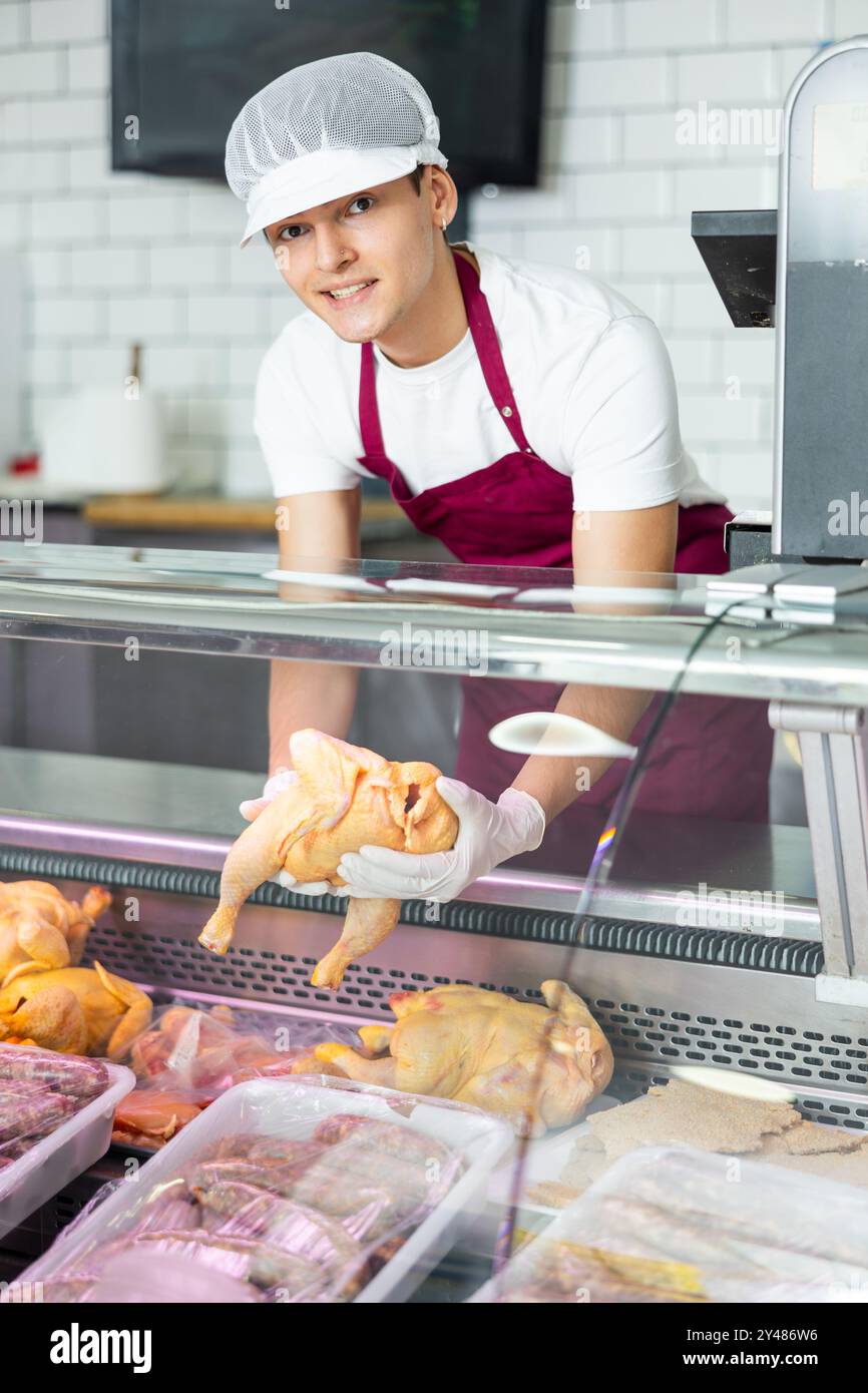 Positive young salesman demonstrating chicken in butcher shop Stock ...