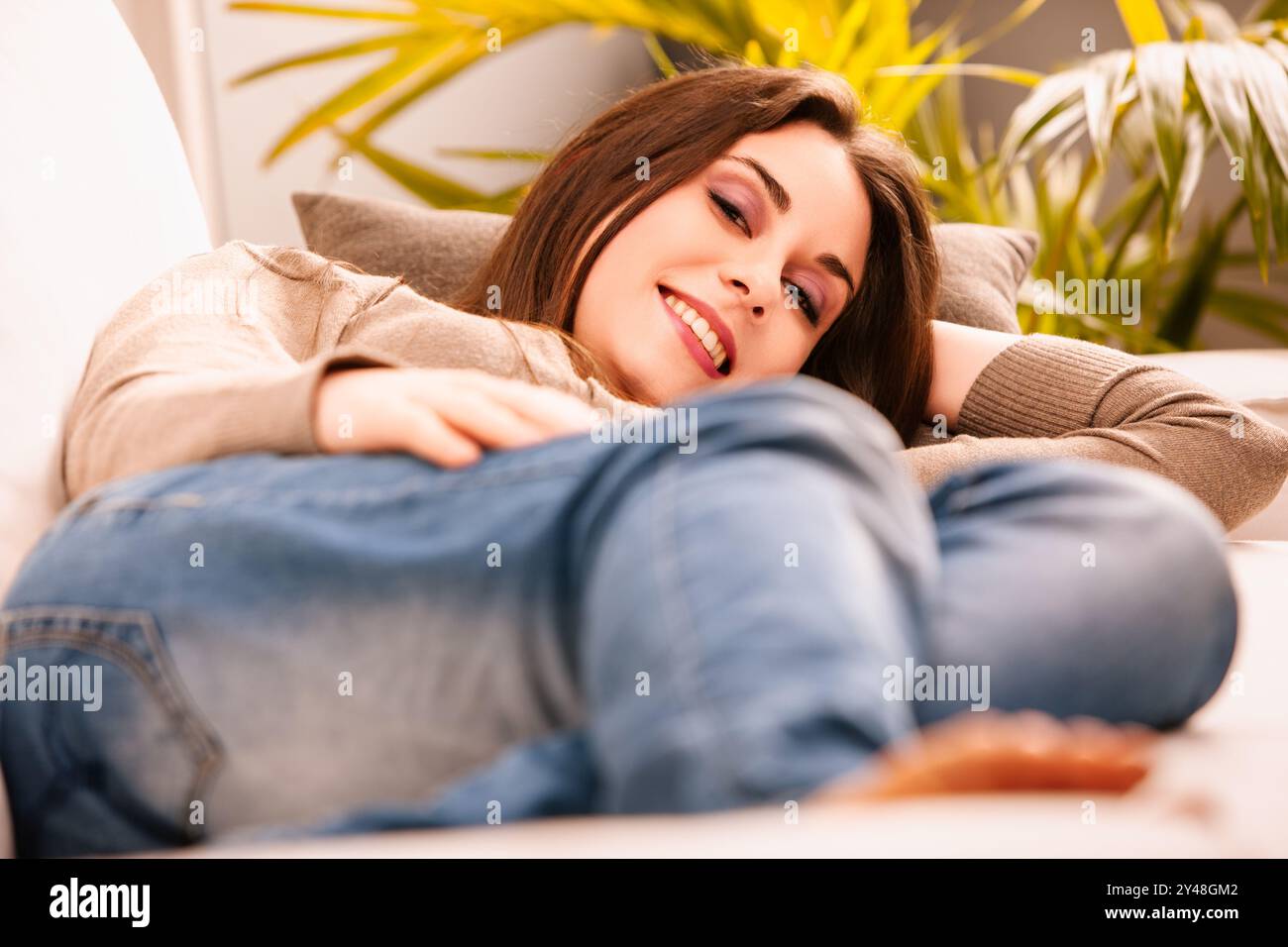 Young woman lies comfortably on her sofa, smiling happily in her cozy ...