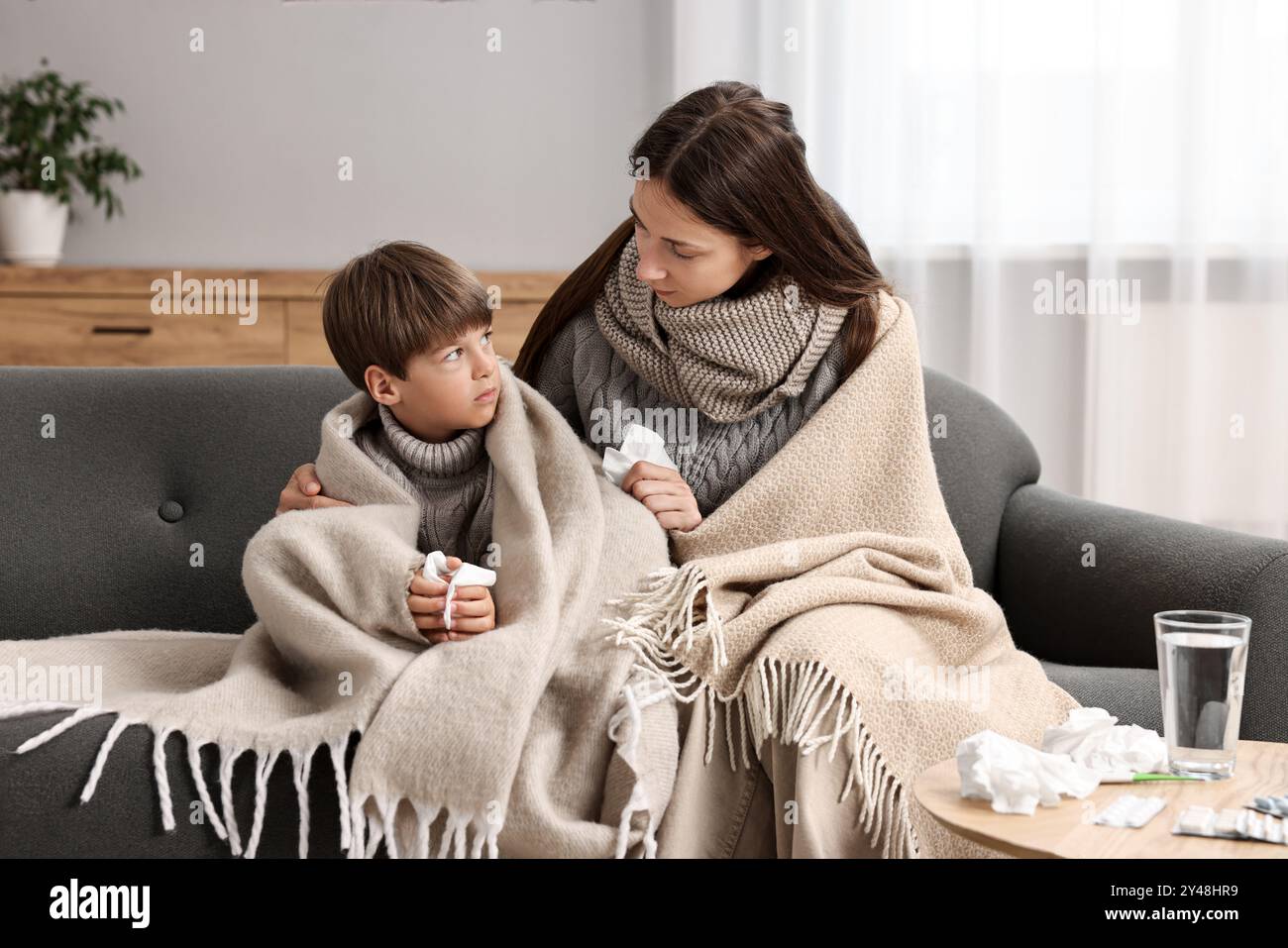 Cold symptom. Woman with her son suffering from fever on sofa at home ...