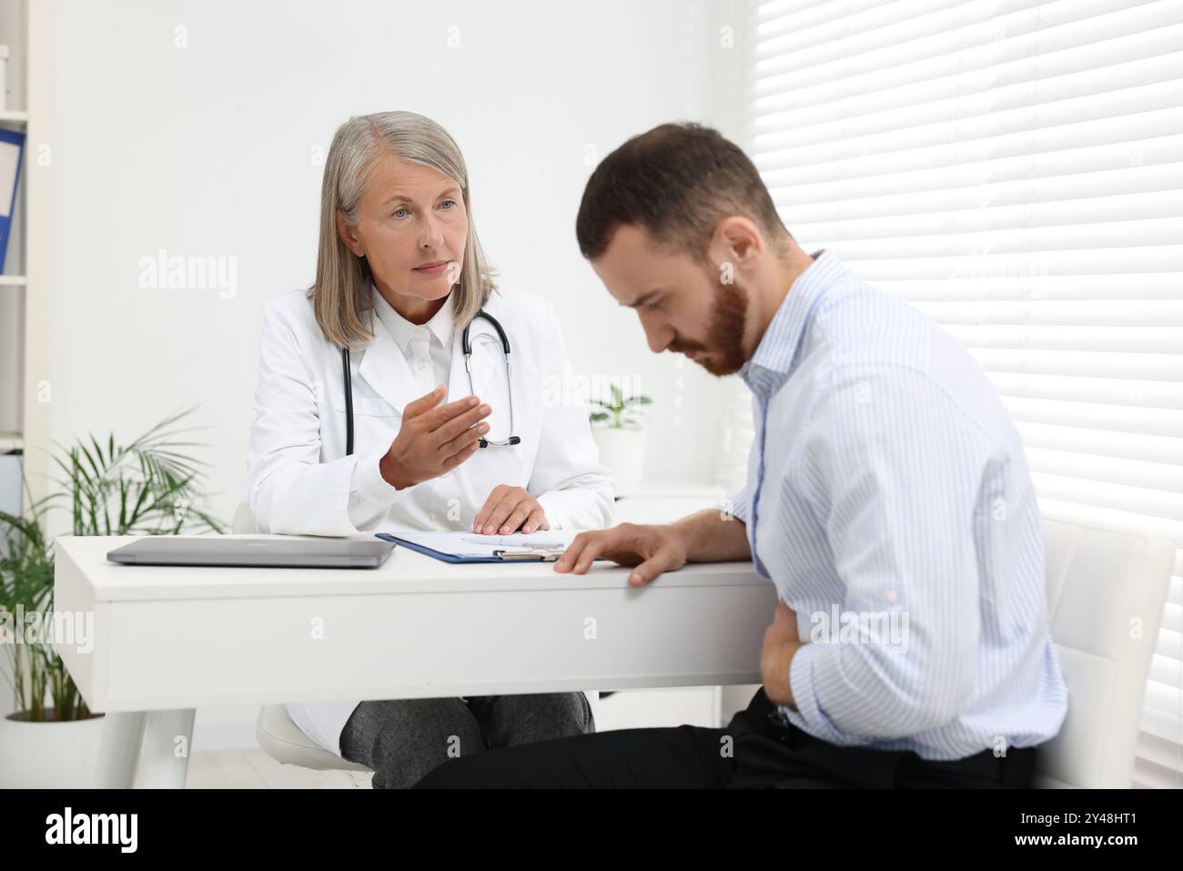 Doctor consulting patient with stomach pain at table in clinic Stock ...