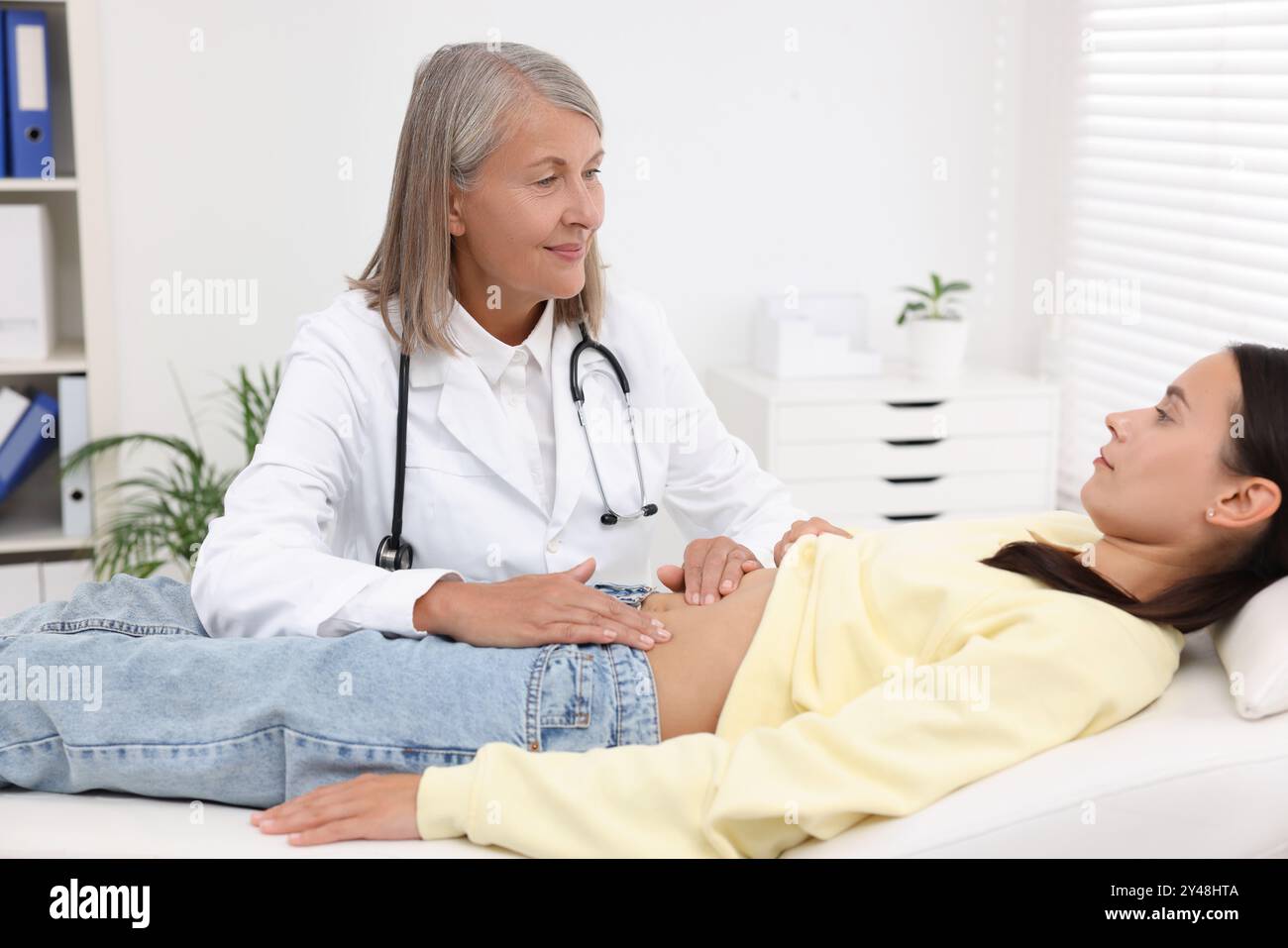 Doctor examining woman with stomach pain on couch in clinic Stock Photo ...