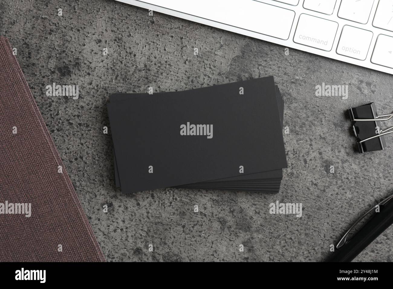 Blank business cards, keyboard and binder clip on grey textured table, flat lay. Mockup for ...