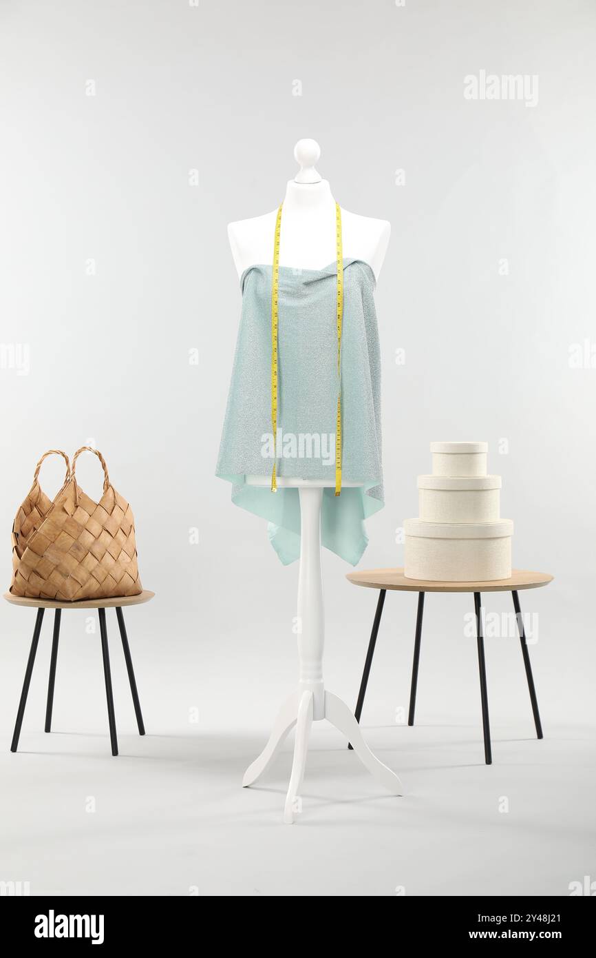 Mannequin with measuring tape, fabric, bag and boxes on side tables ...