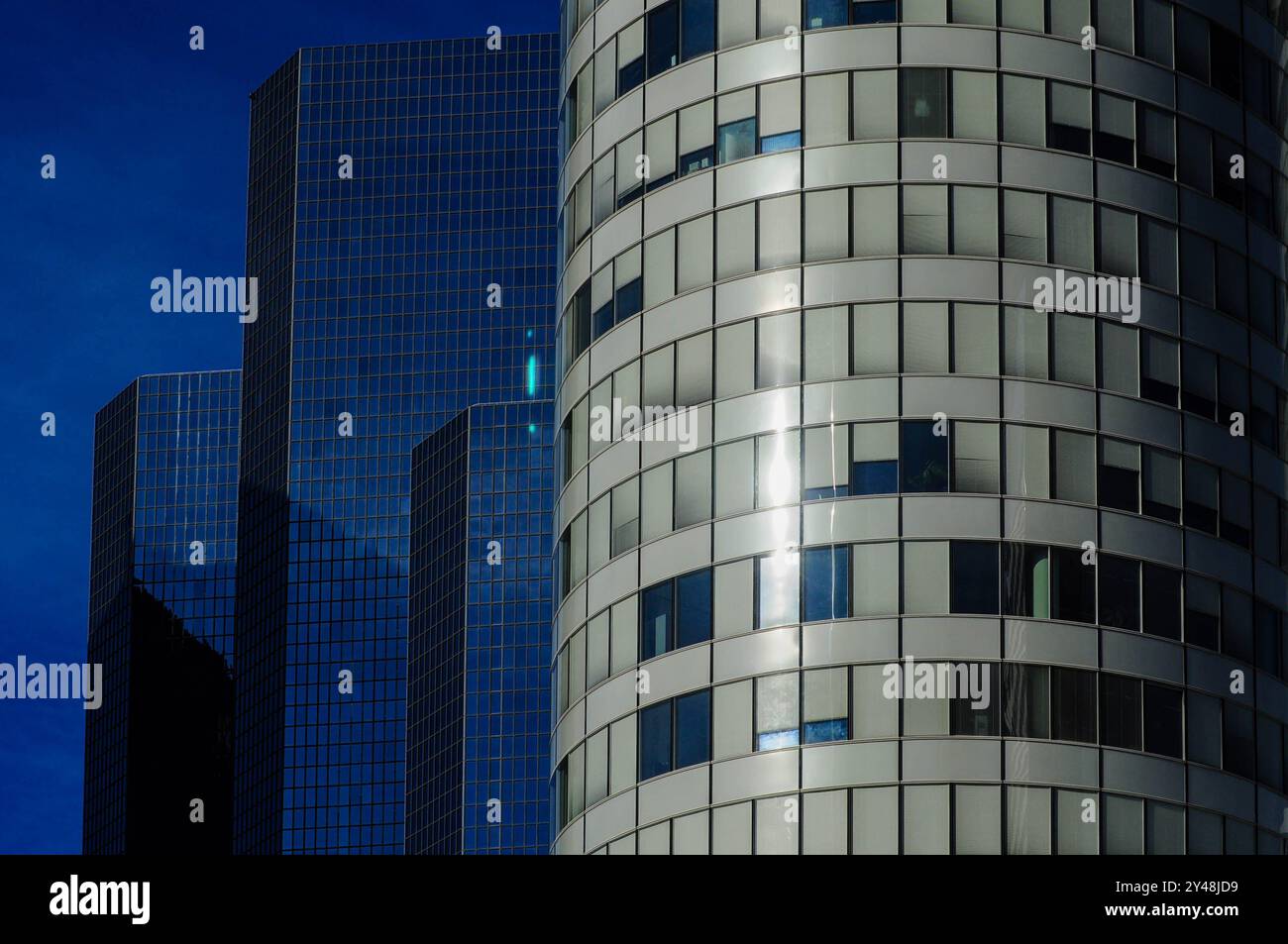 Modern skyscrapers and tiled cylindrical building against blue sky ...