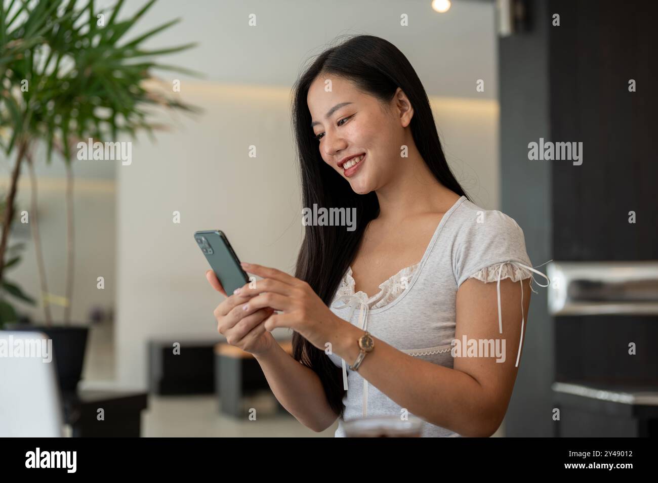 A beautiful, positive Asian woman using her smartphone while sitting in a modern coffee shop ...