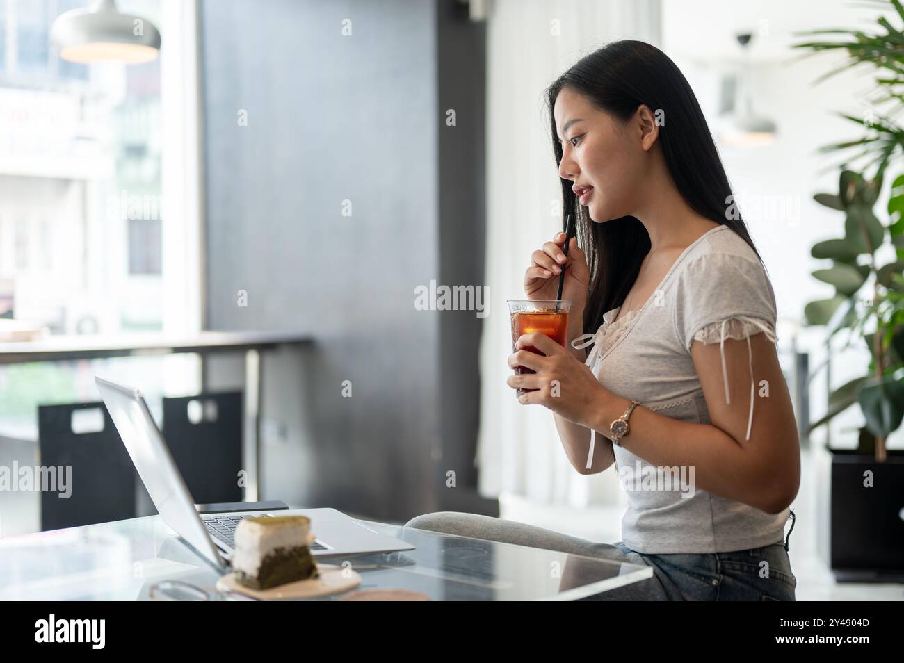 A side view of a beautiful Asian woman sipping iced americano while ...