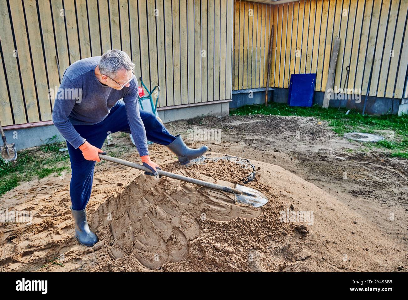 Builder compacts sand near septic tank manhole cover, patting its ...