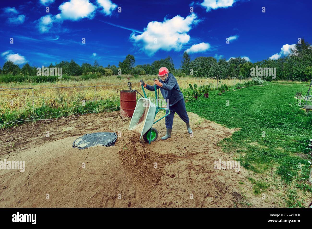 Worker buries concrete rings of septic tank with sand, pouring it out ...