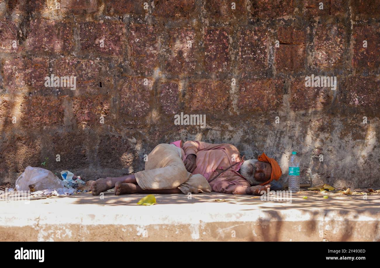 GOA, India - February 21, 2024: An old man in dirty clothes lies on the ...
