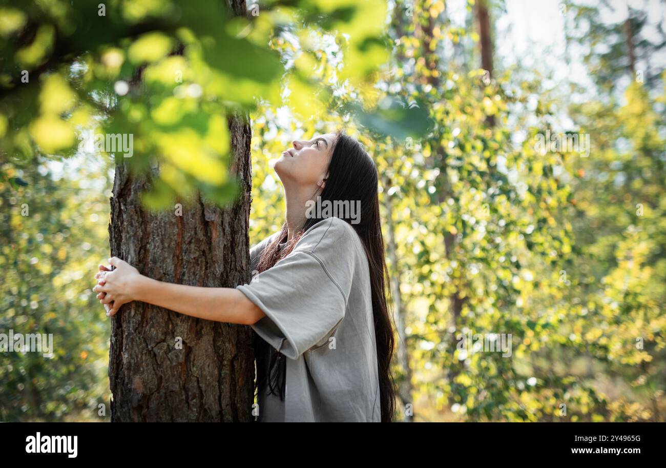 A woman leans against a tree, gazing upwards with a serene expression ...