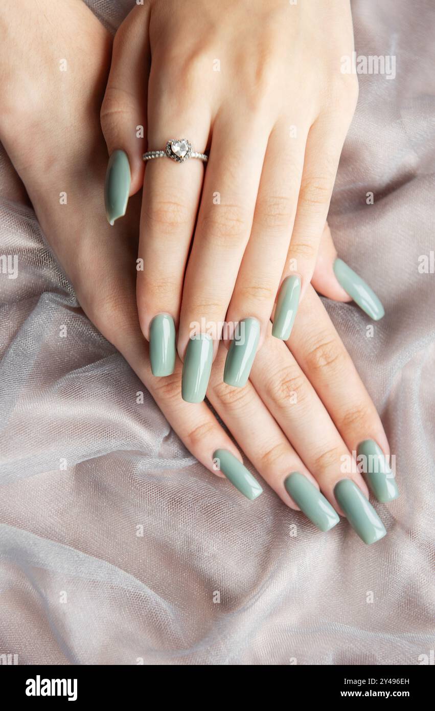 A pair of hands with long, manicured fingernails painted a light shade ...