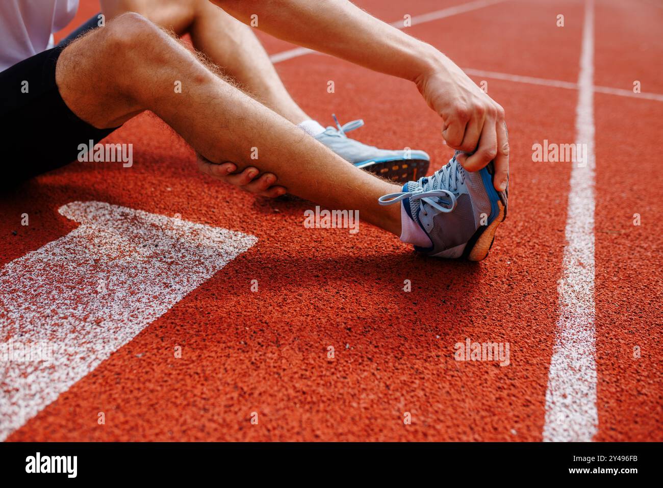 Athlete stretching on a running track, focusing on legs and shoes Stock ...