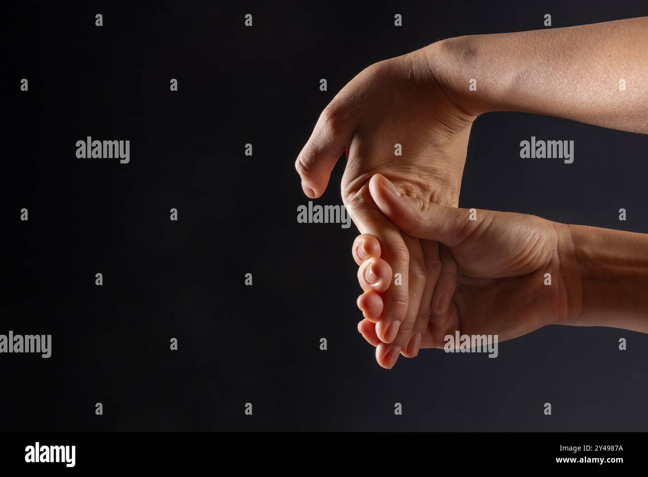 close up of female hands doing wrist stretching on dark background ...