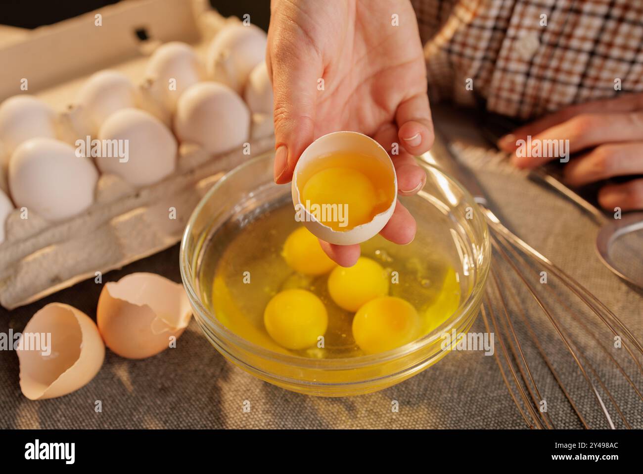 A person cracking an egg into a glass bowl, with several eggs in an egg ...