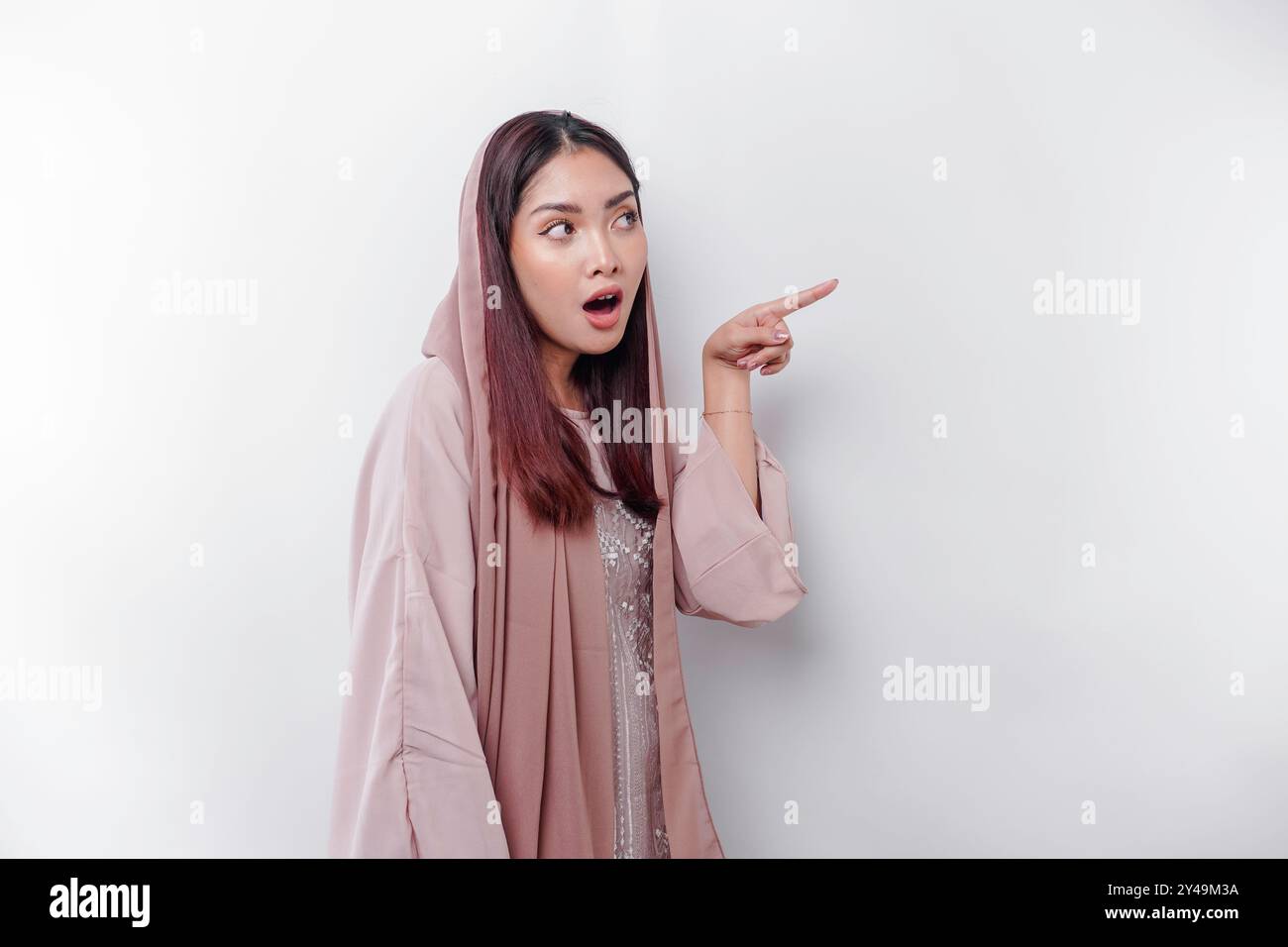 Shocked Asian Muslim woman pointing at the copy space on beside her ...
