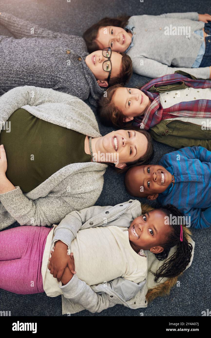 Happy children, portrait and teacher lying above with students on floor ...