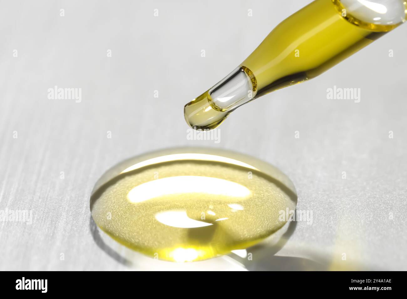 Cosmetic oil dripping from pipette on light grey background, closeup ...