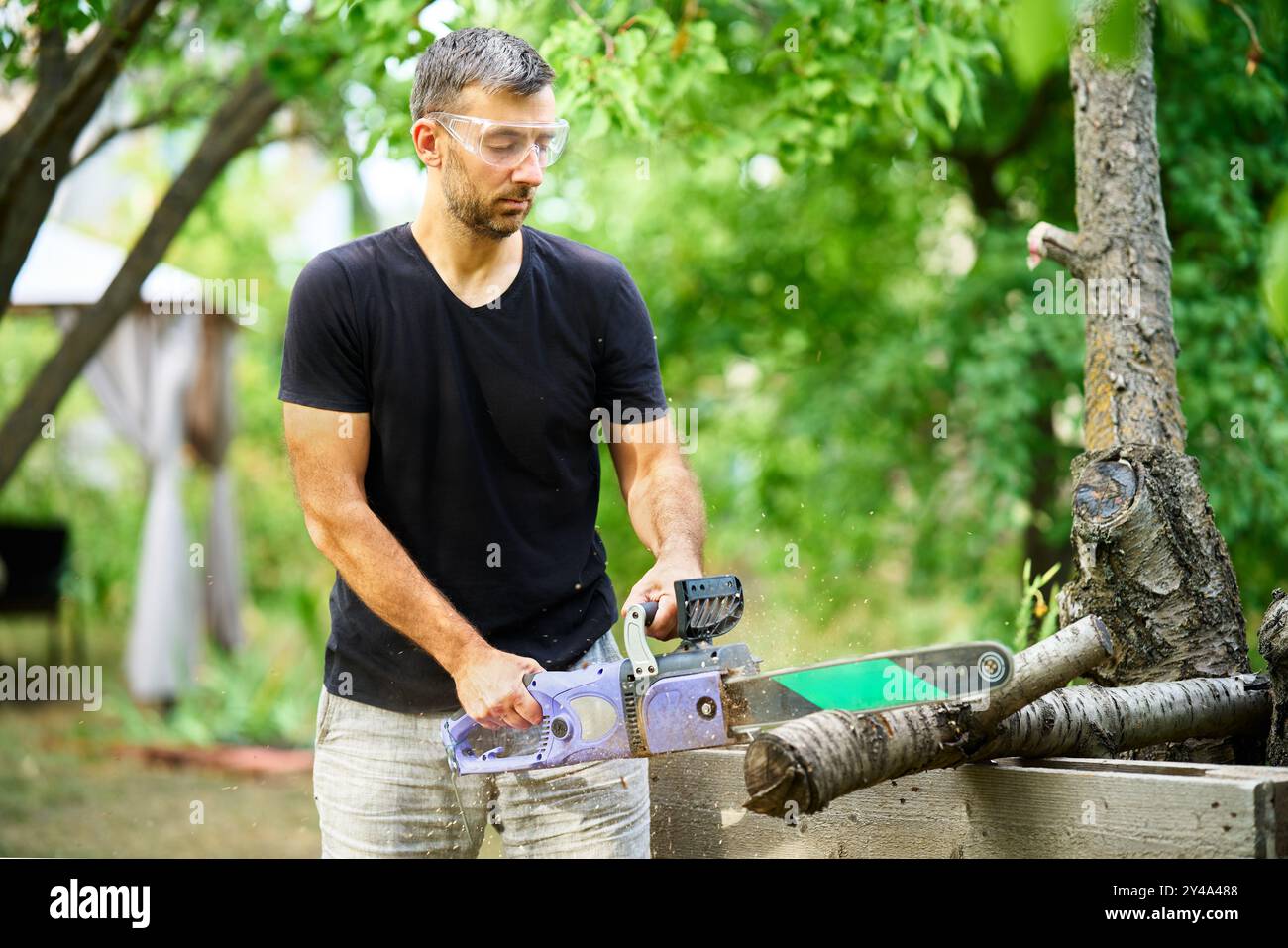 Young man using chainsaw for cutting tree branches at his backyard ...