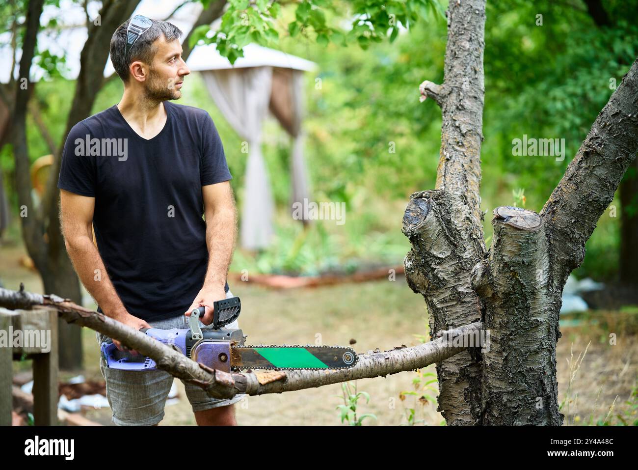 Handsome man using chainsaw for cutting tree branches at his backyard ...