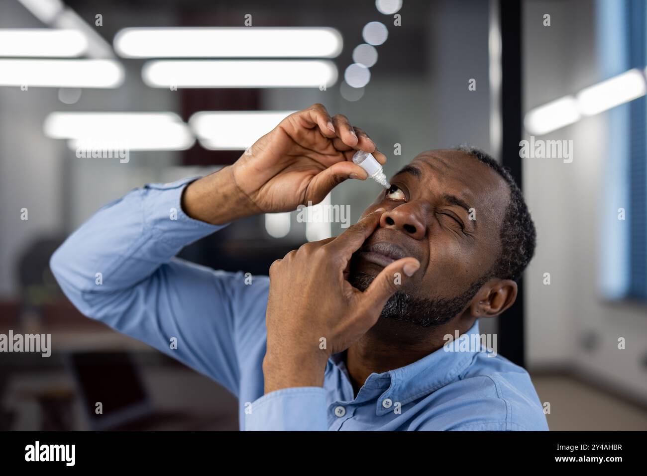 African American mature businessman applying eye drops to relieve ...