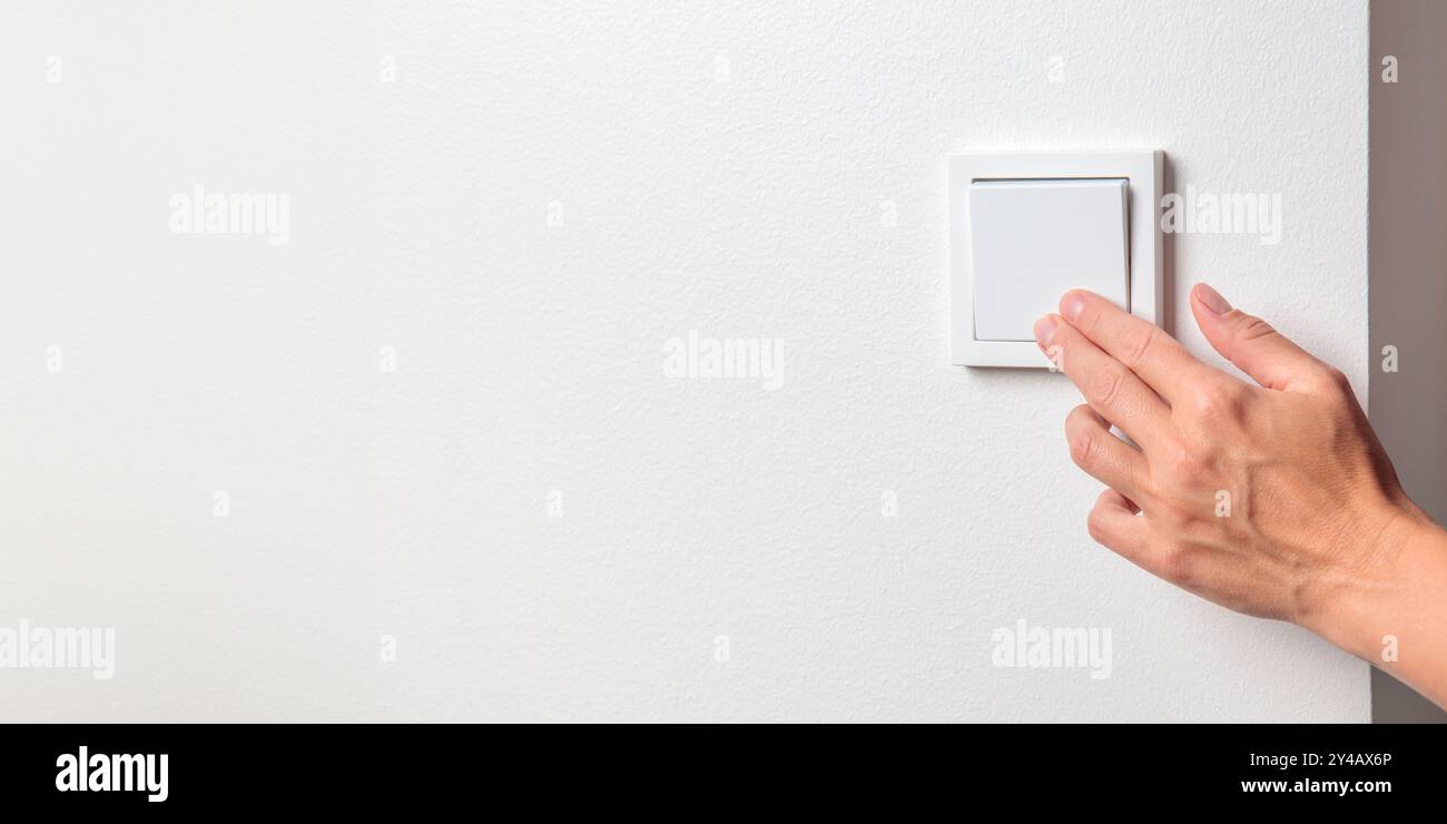 A woman's hand turning off a light switch on a white wall. The ...