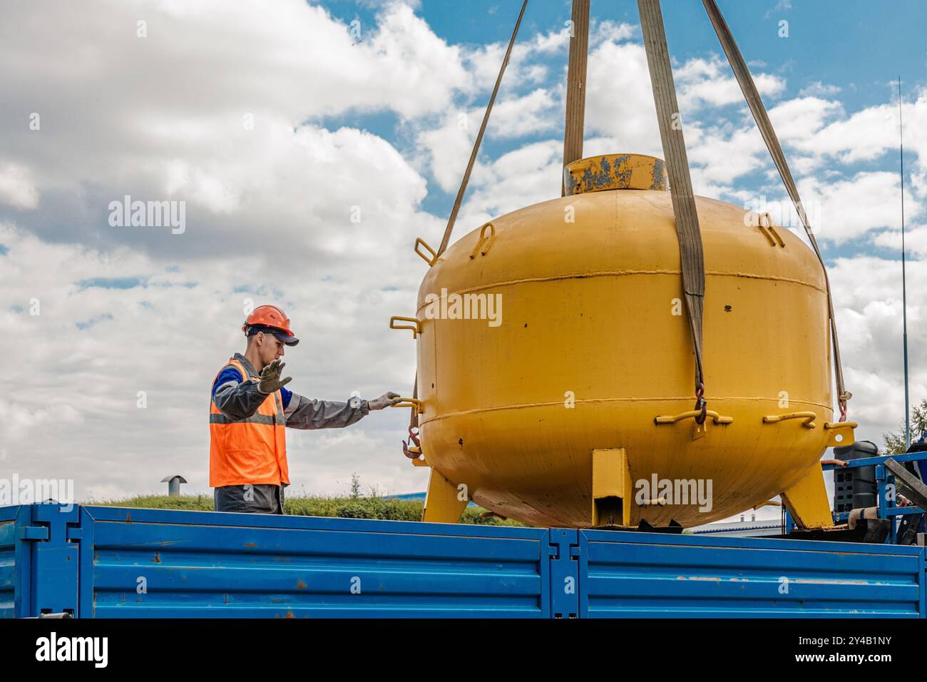 A construction worker in safety gear securing a large yellow industrial ...