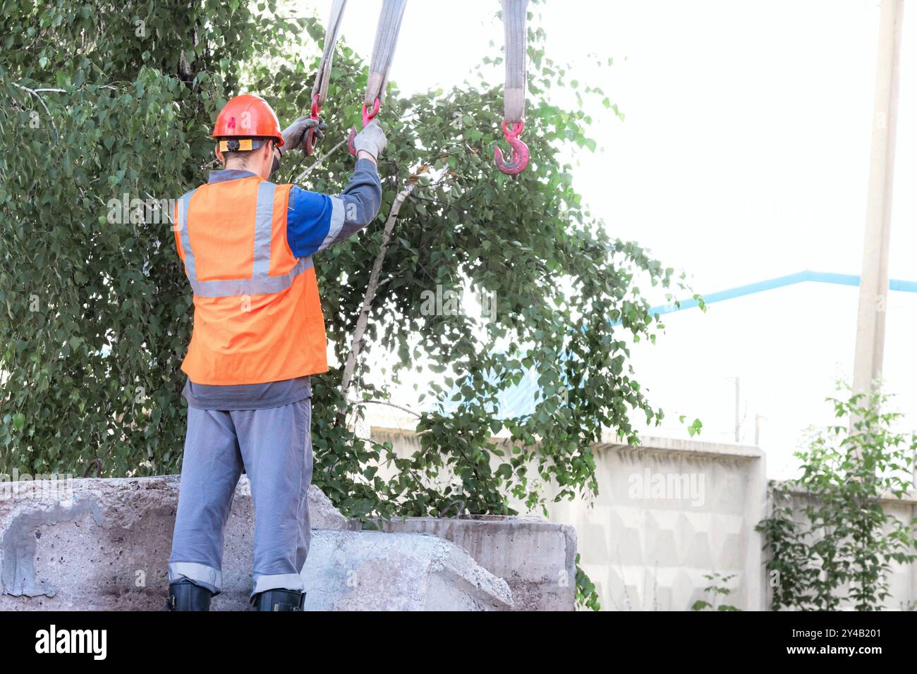 Construction worker in orange vest and hard hat operating crane to lift ...