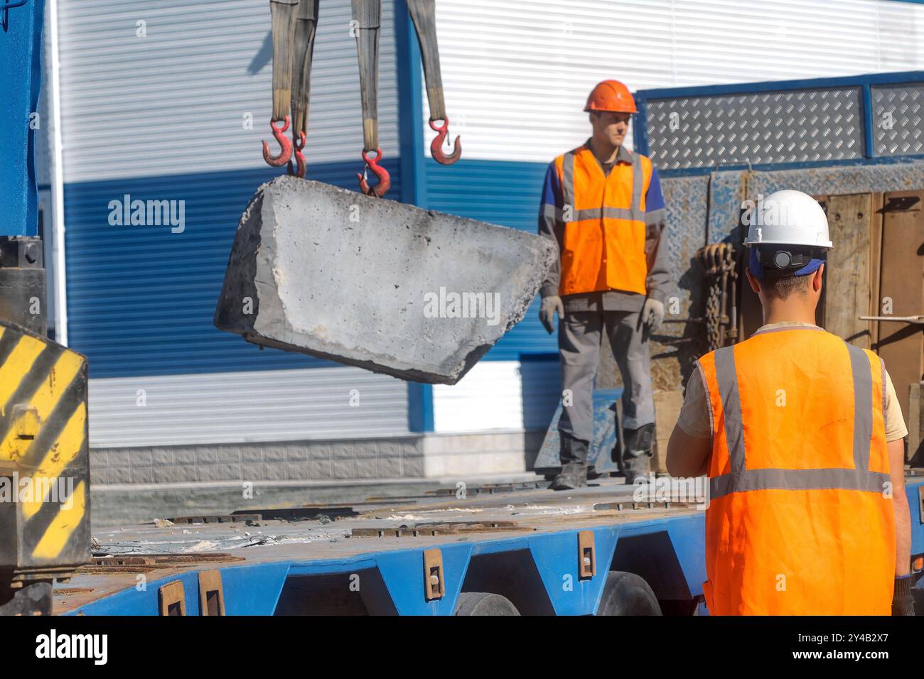 Construction worker overseeing the hoisting of a massive concrete block ...
