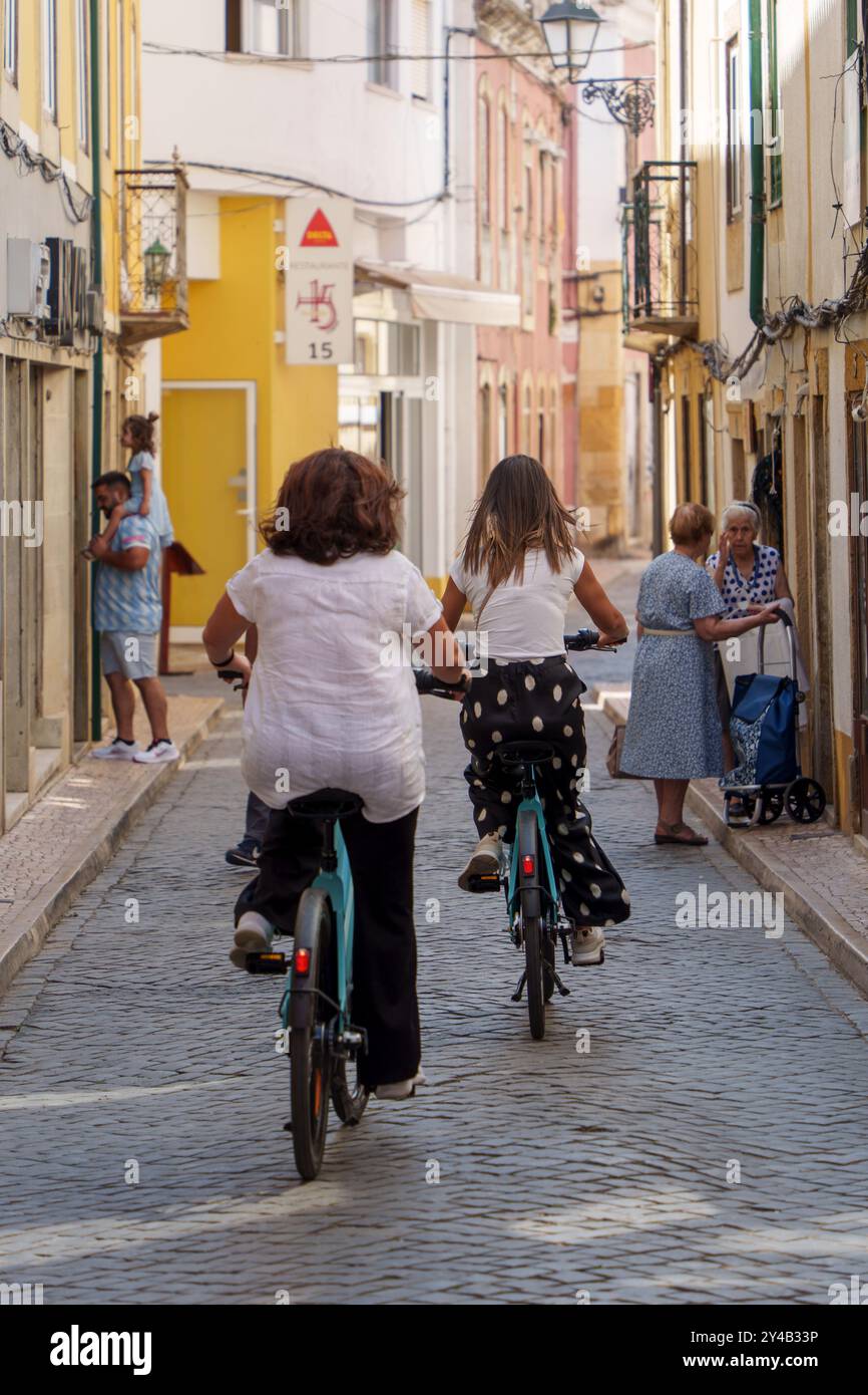 Two people riding bicycles on a cobblestone street in Tomar, Portugal ...
