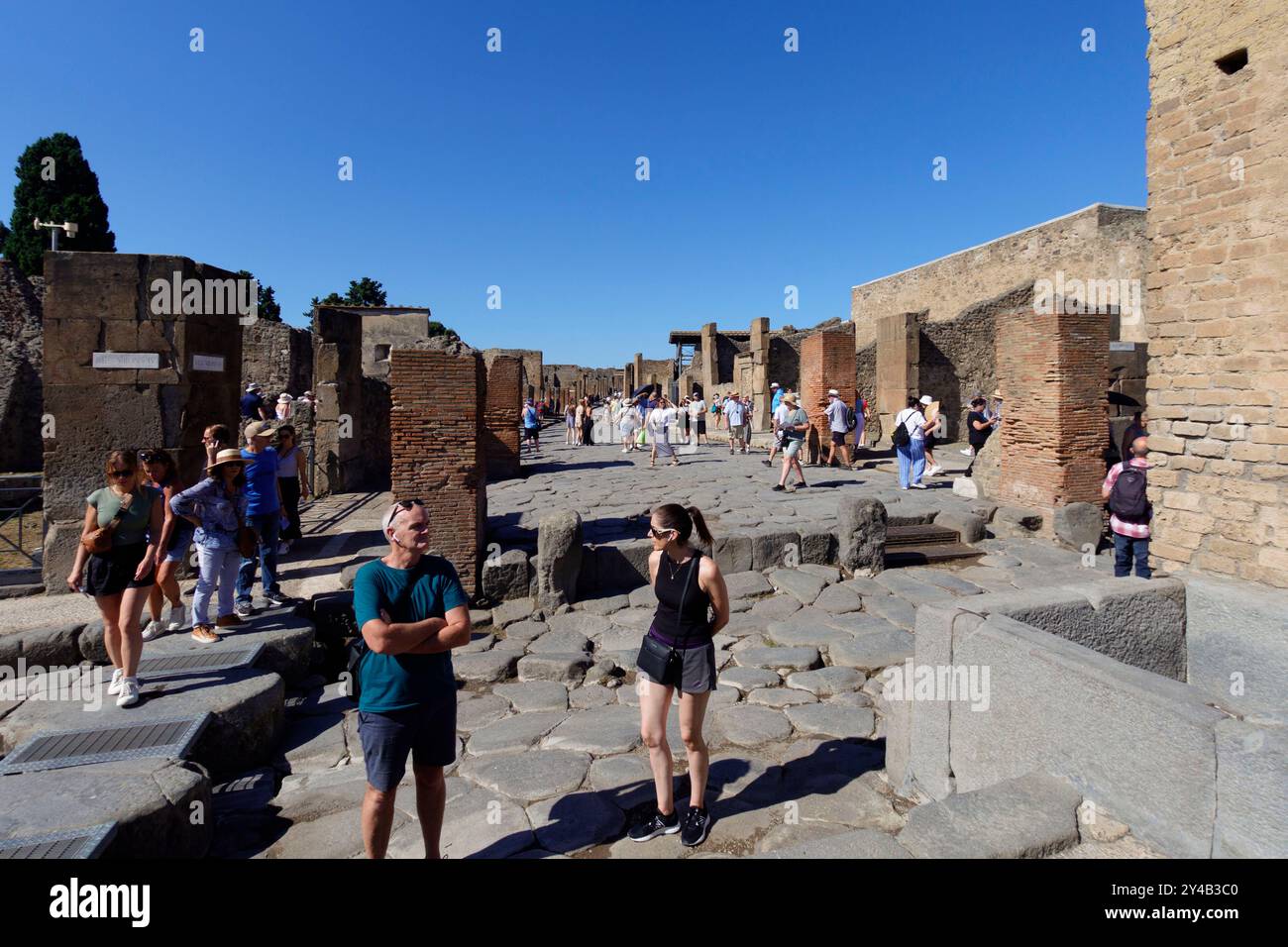 Tourists exploring ancient ruins in Pompeii under a clear blue sky with historical structures ...