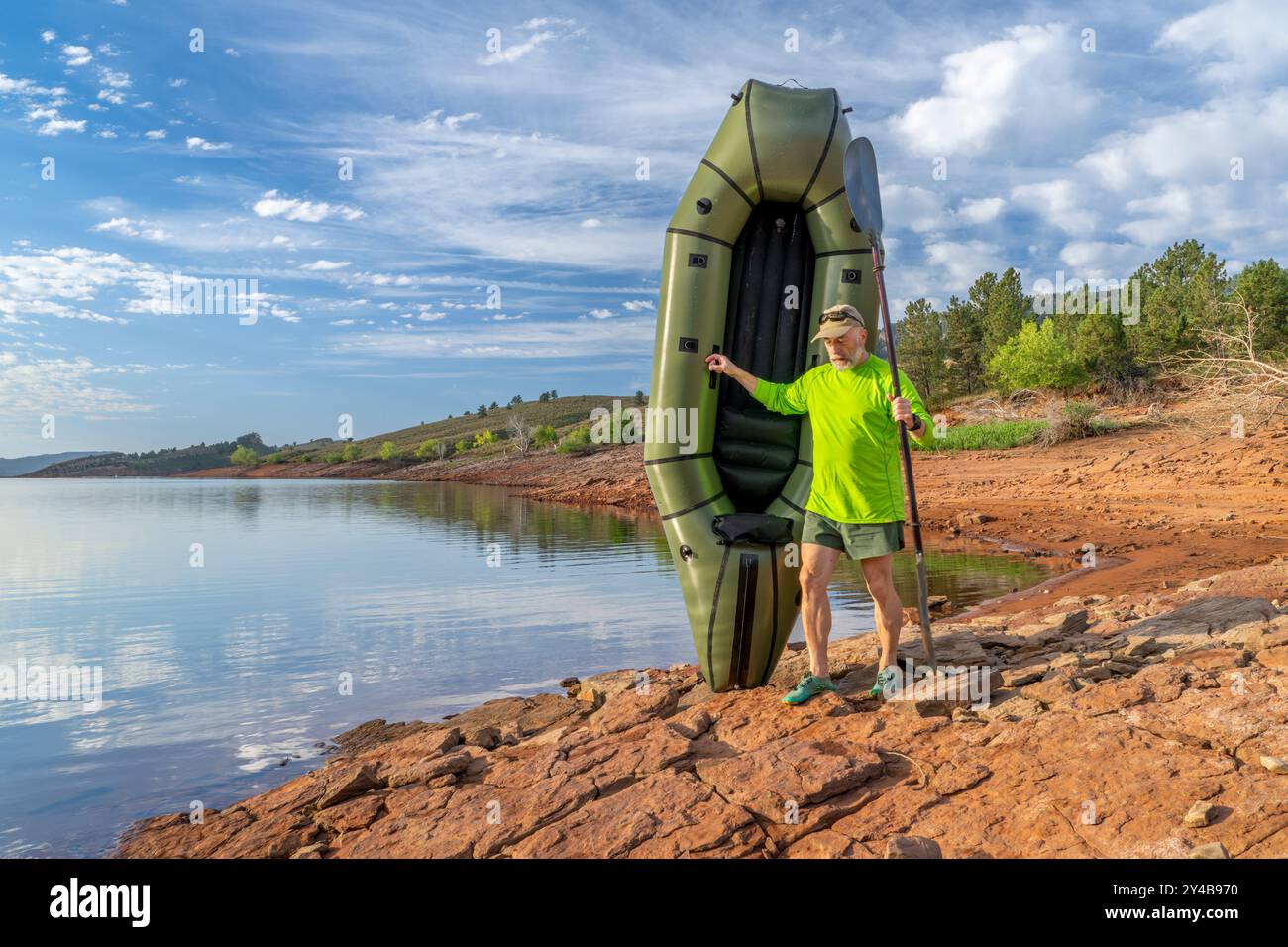 senior male paddler is launching an inflatable packraft on a shore of ...