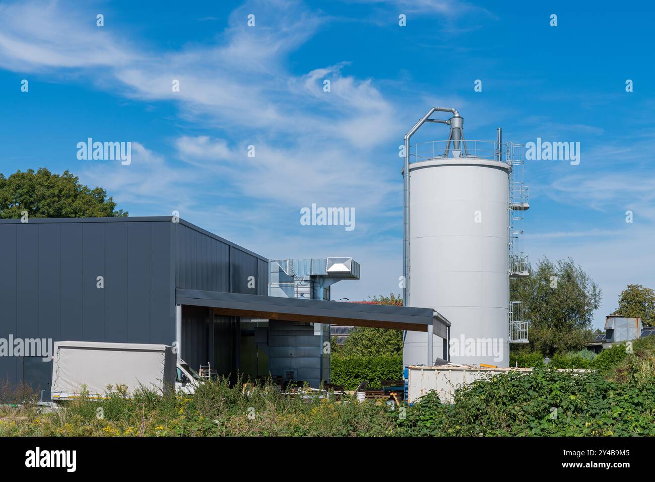 A contemporary industrial building sits beside a tall silo, surrounded ...