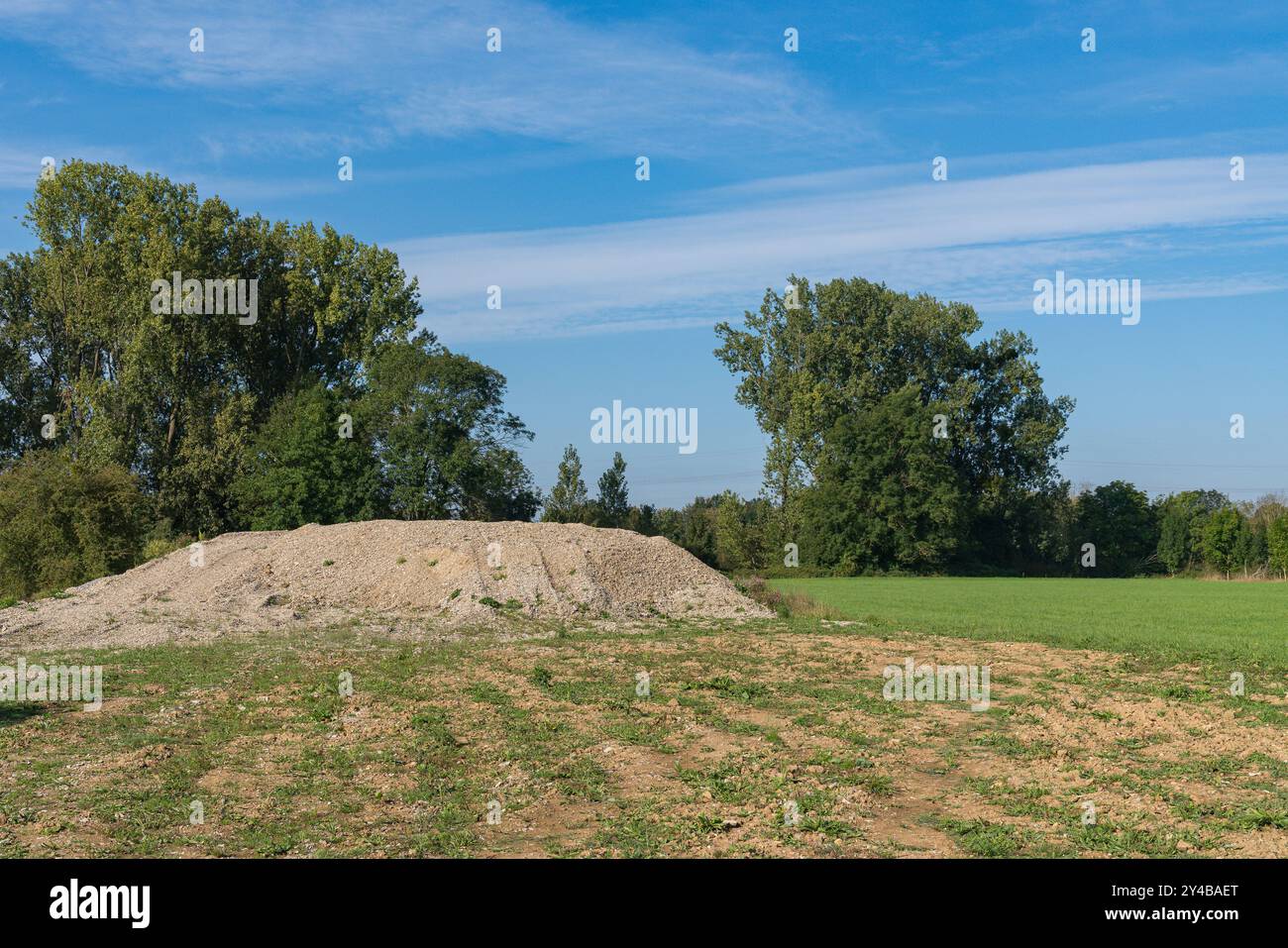 A gravel mound rises amidst lush green grass under a clear blue sky ...