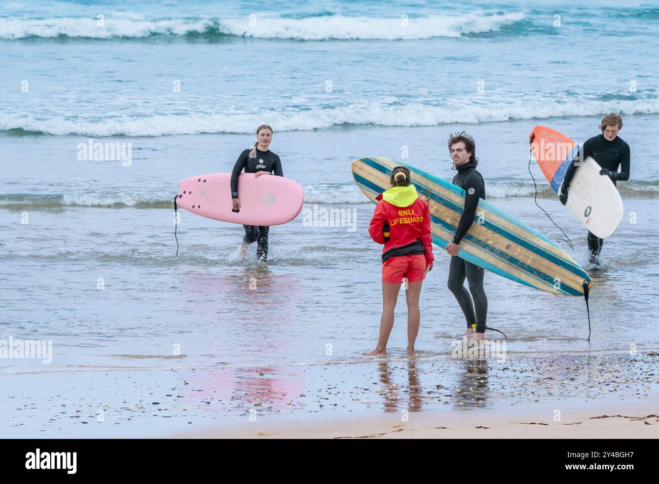 A female RNLI Lifeguard giving safety advice to surfers on Fistral ...