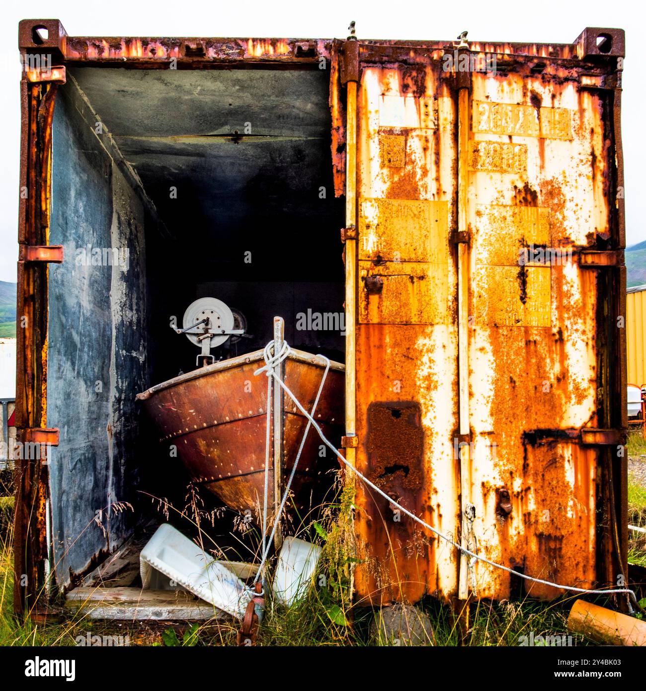 small abandoned fishing boat inside a rusty container with half open ...