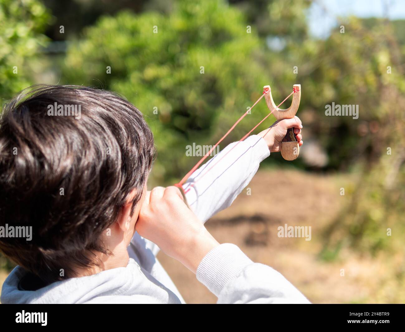 Boy aiming a slingshot in a sunny outdoor environment Stock Photo - Alamy