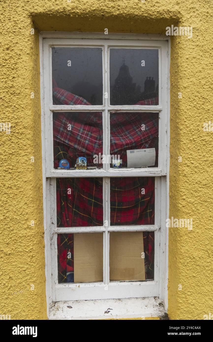 A window in a yellow wall with a red chequered curtain and small ...