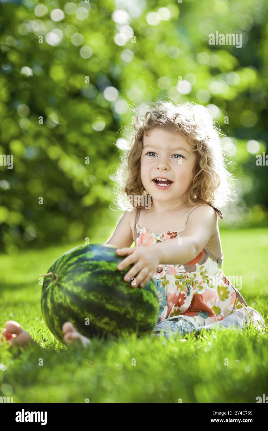 Happy child playing with watermelon against green spring background ...