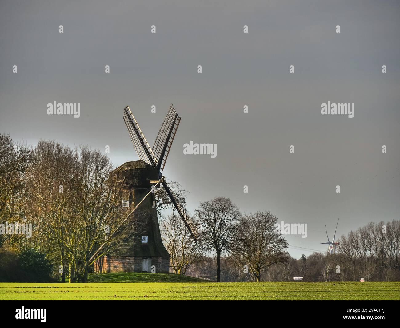 Old windmill surrounded by trees and a field under a cloudy sky ...